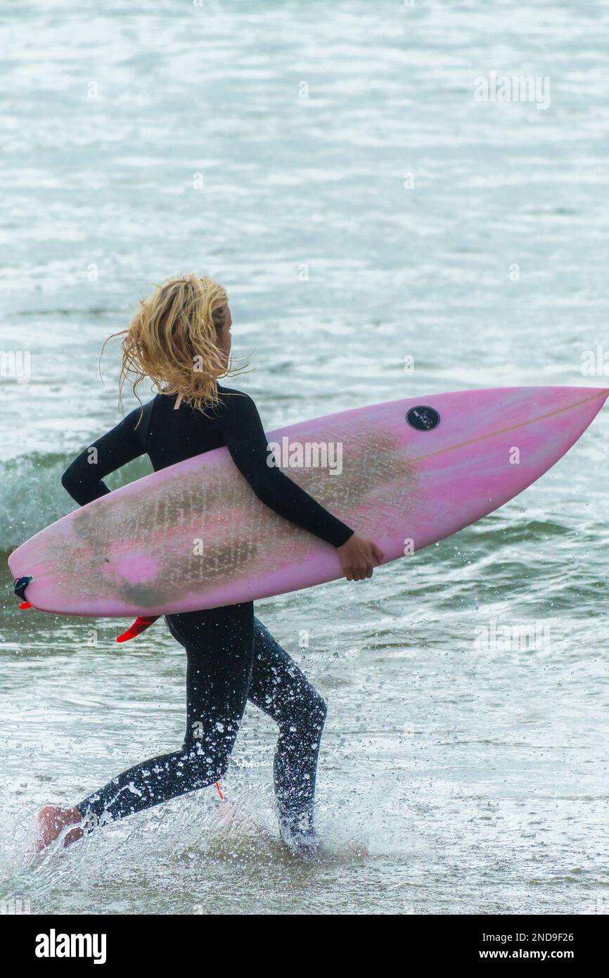 An eager young female surfer carrying her colourful surfboard running ...