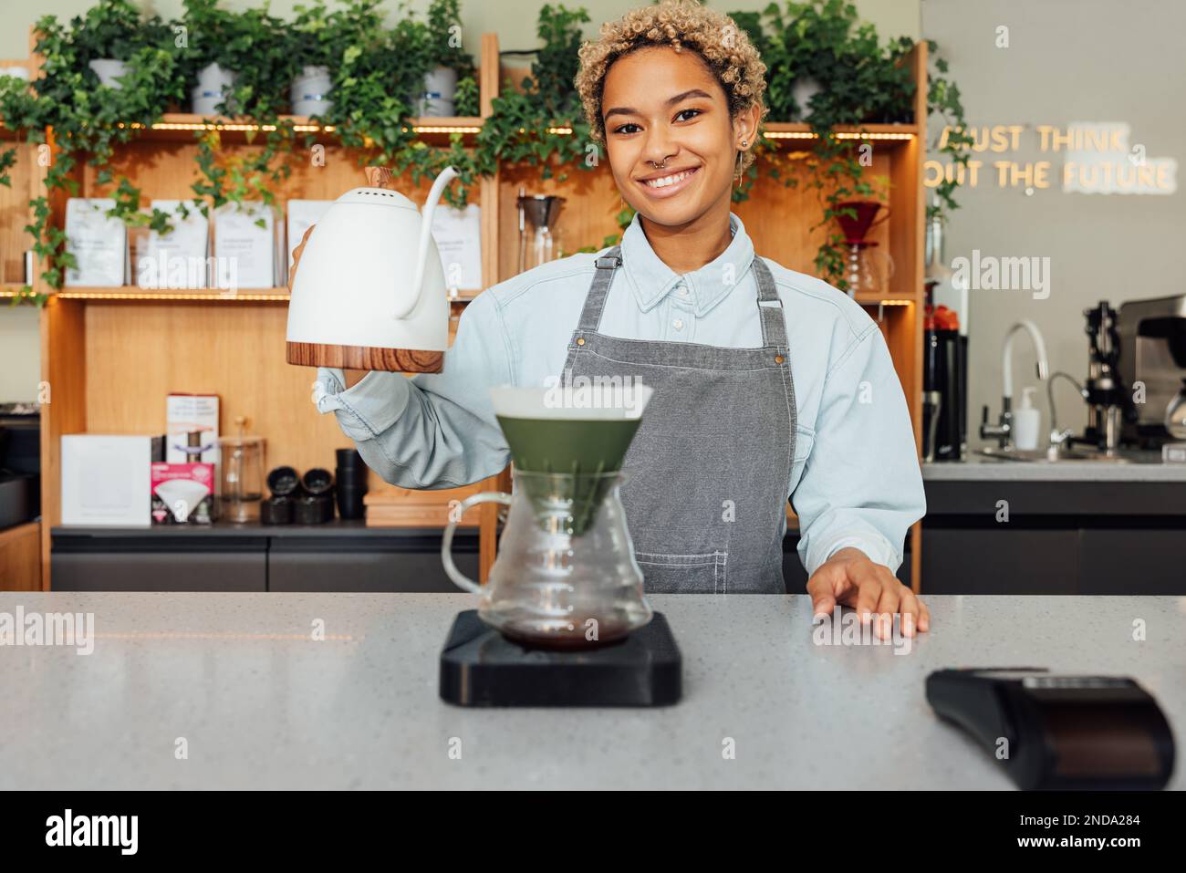 Smiling female barista holding a kettle while standing at a counter in ...