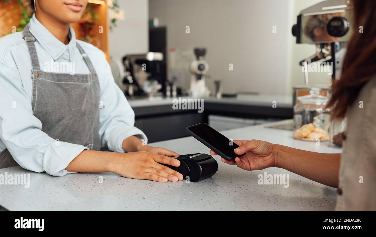 Unrecognizable customer paying by NFC at a cafe. Barista holding pos ...