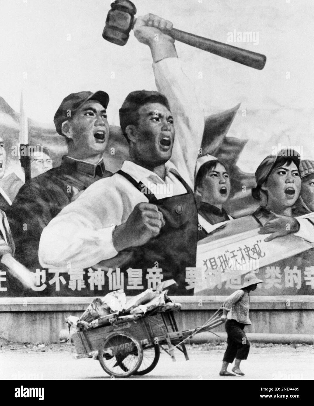Chinese woman pulls a cart past a huge poster depicting a worker ...