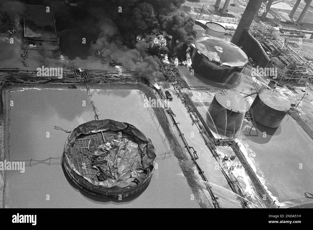 Oil tank collapsed at lower left and fire burning on and around tank at ...