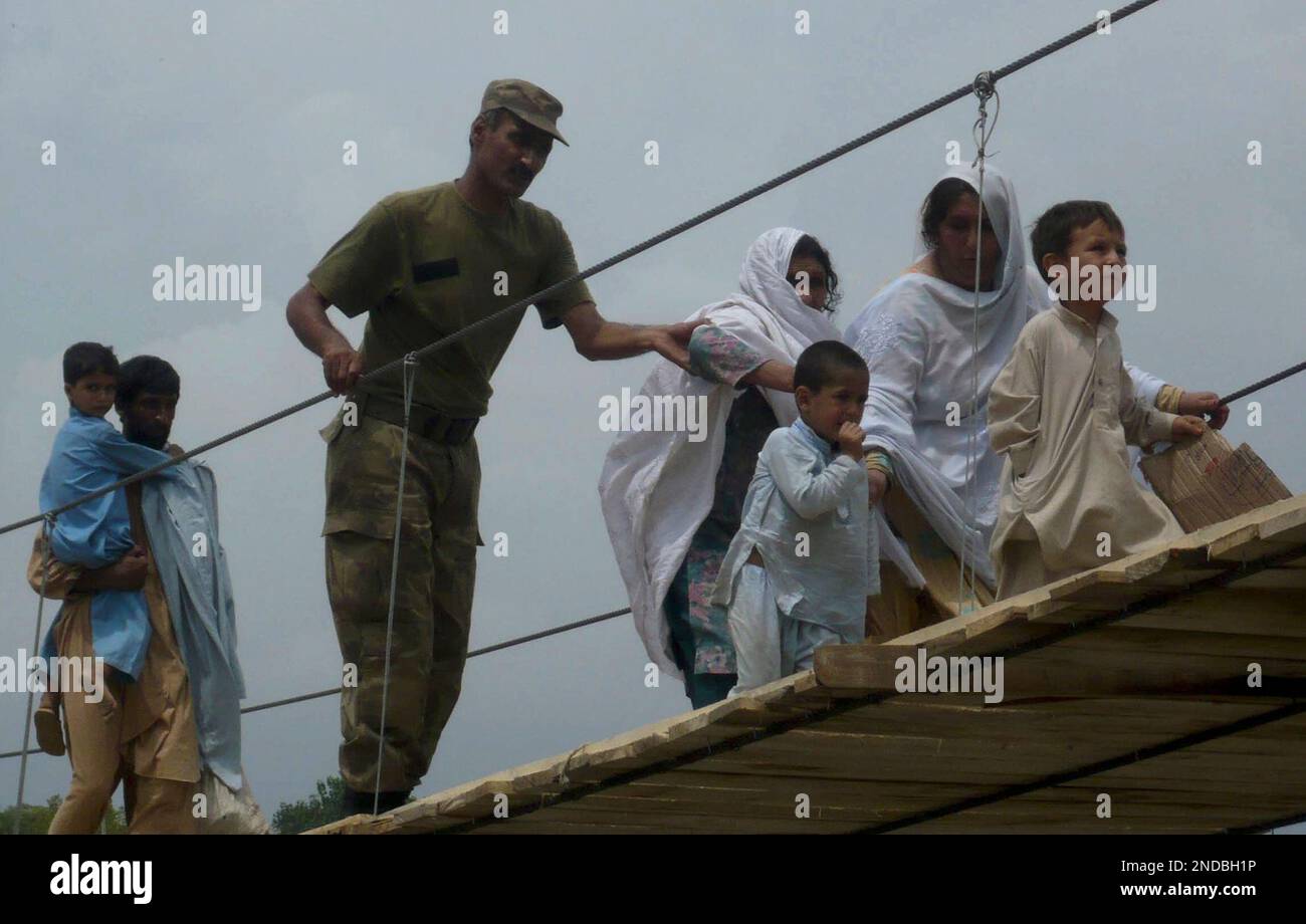 A Pakistan army soldier helps people affected by floods walk over a ...