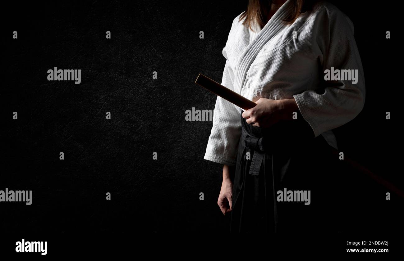 A woman in black hakama standing in fighting pose with wooden sword ...