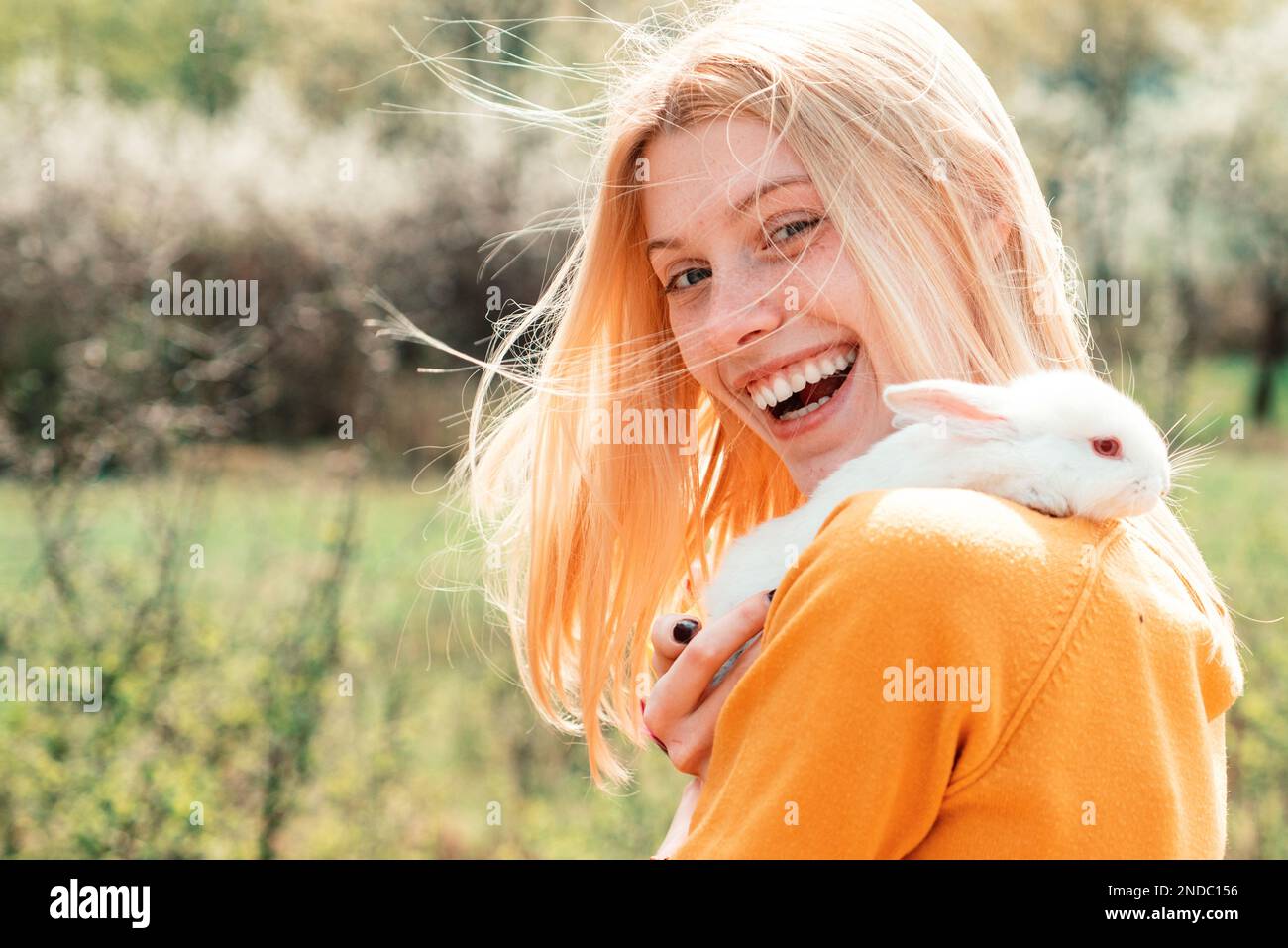 Funny girl hold rabbit on green field background. Closeup of winking ...