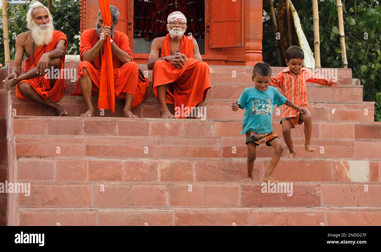 Children run past Sadhus, or Hindu holy men, sitting on the banks of ...