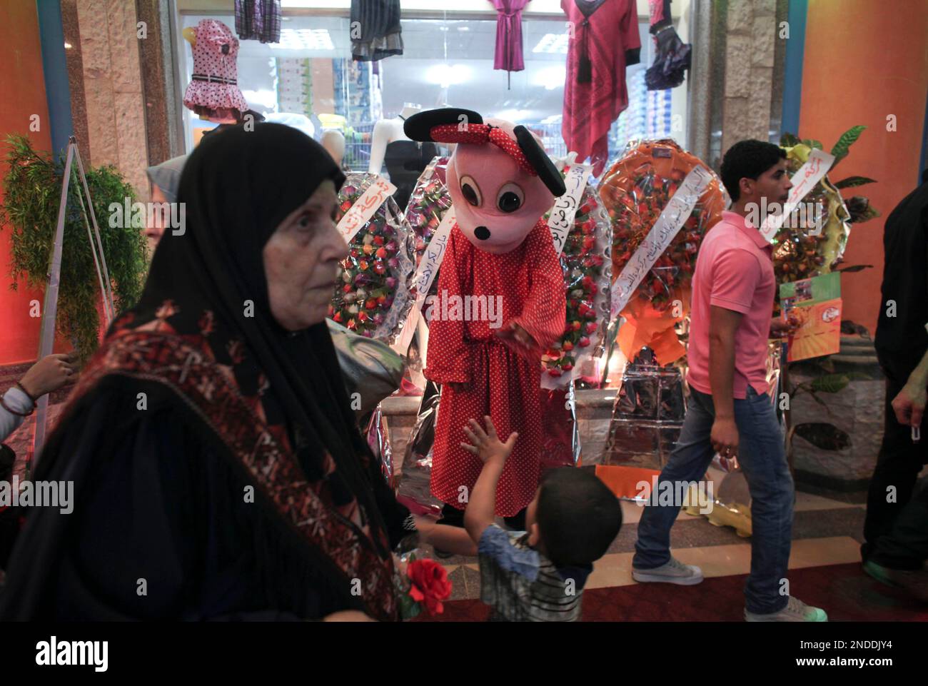 A Palestinian child waves to a woman dressed up as a large mouse as ...