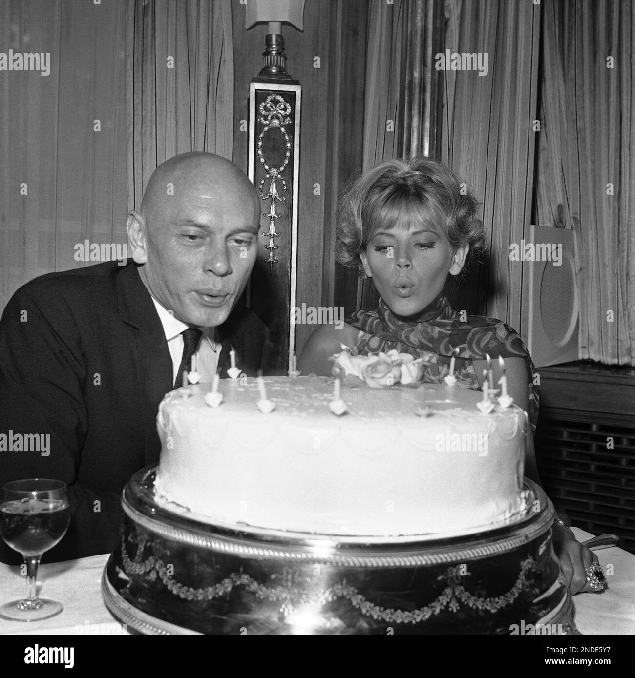 Sitting behind a big birthday cake Swedish actress Britt Ekland helps American film actor Yul ...