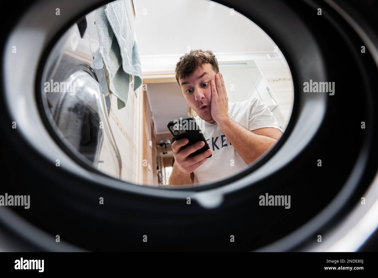Man with mobile phone, view from washing machine inside. Male does ...