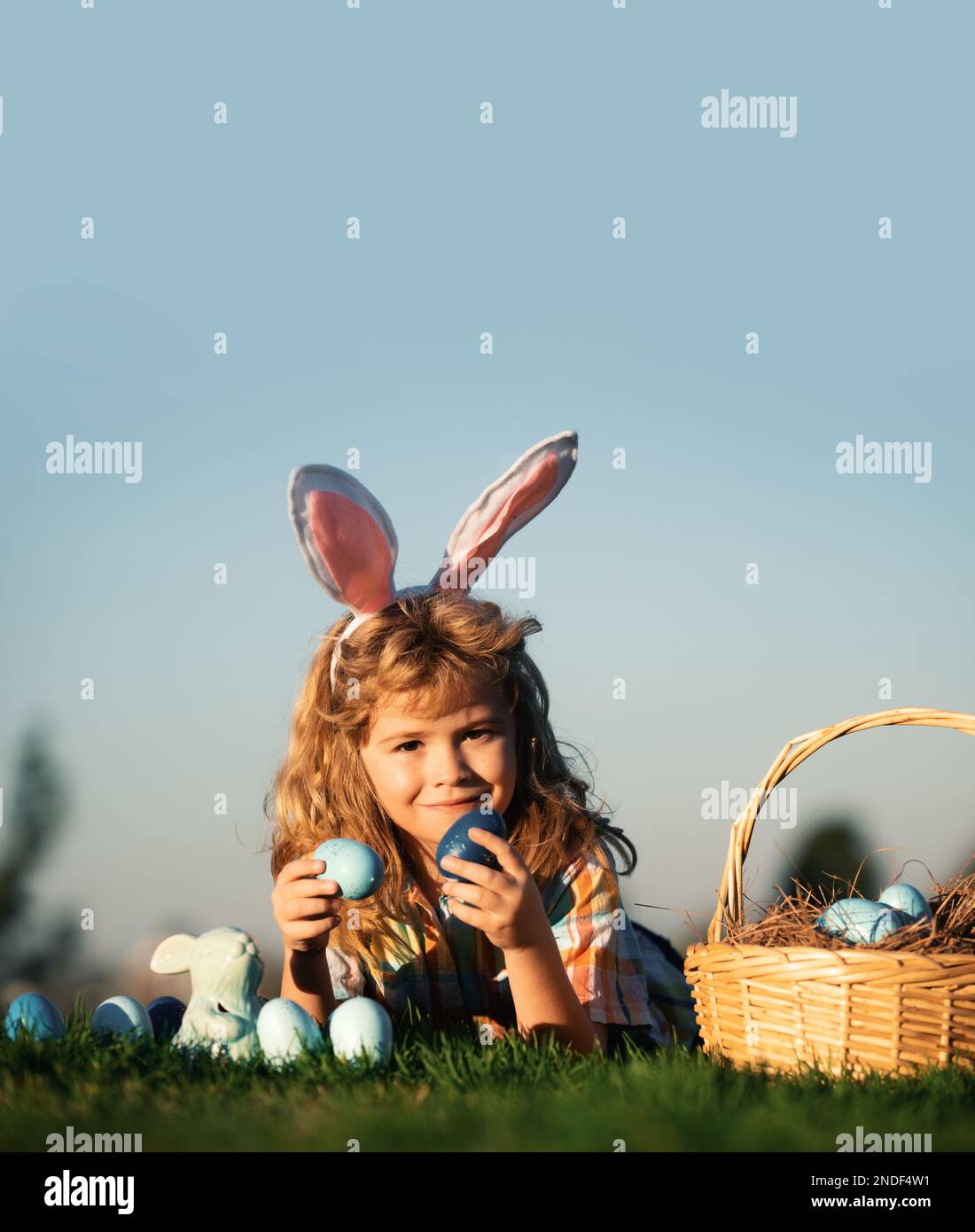 Child with easter eggs in basket outdoor. Boy laying on grass in park ...