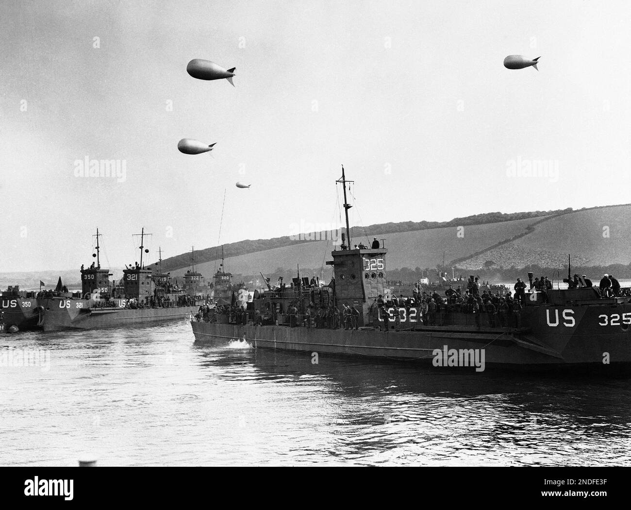 Landing craft loaded with American troops and with barrage balloons ...