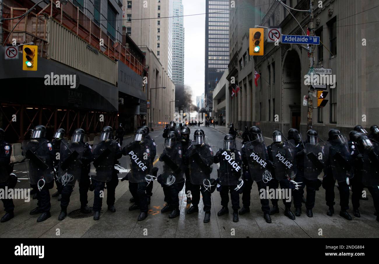 A line of riot police block Bay Street in Toronto as a squad car burns ...