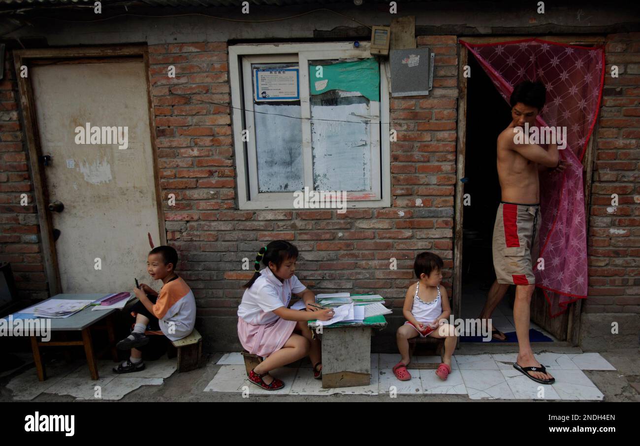 A Chinese man, right, walks out of his house, as children sit doing ...