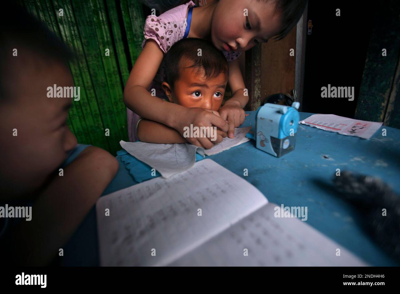 A Chinese girl shows a younger child how to write while doing their ...