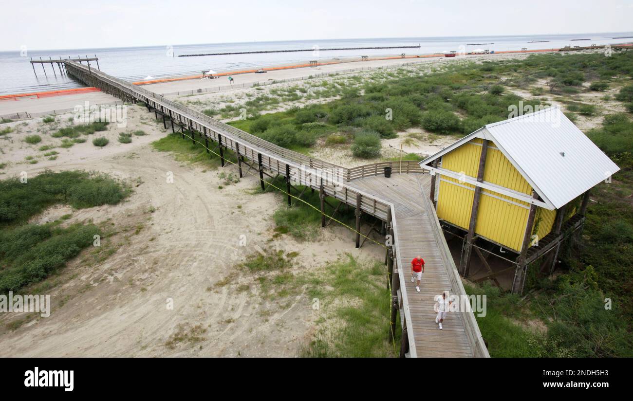 Visitors walk off an empty pier as booms cleaning oil from the ...