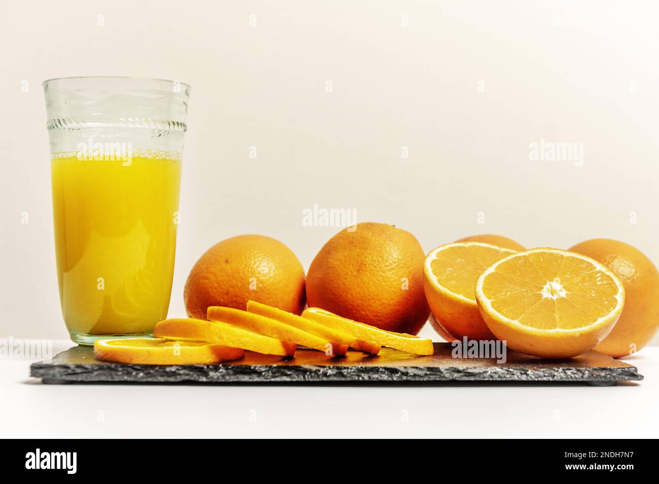 A bunch of ripe oranges with slices and split oranges next to a glass ...