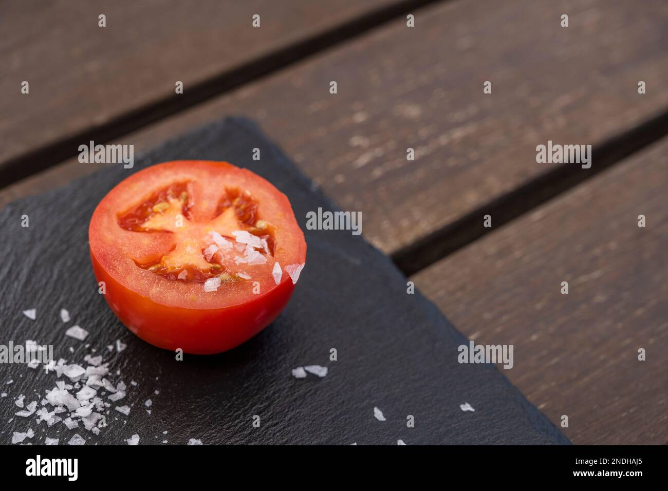 Half ripe tomato halved with flakes of ripe salt on a shiny black slate ...