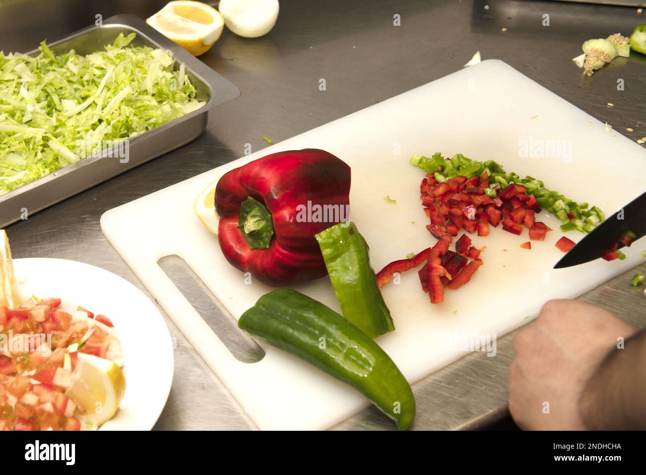 A chef chopping red and green bell peppers on a white Teflon board ...