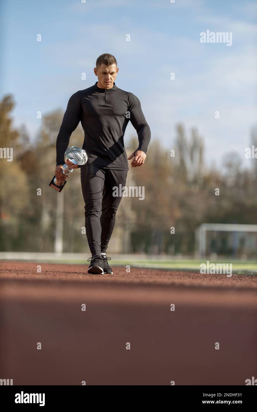 Athletic man walking through the stadium with victory cup Stock Photo ...