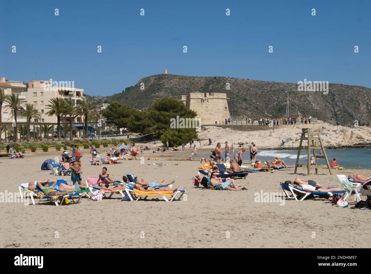Sunbathers lying on beach, Castillo de Moraira,in background, Moraira ...