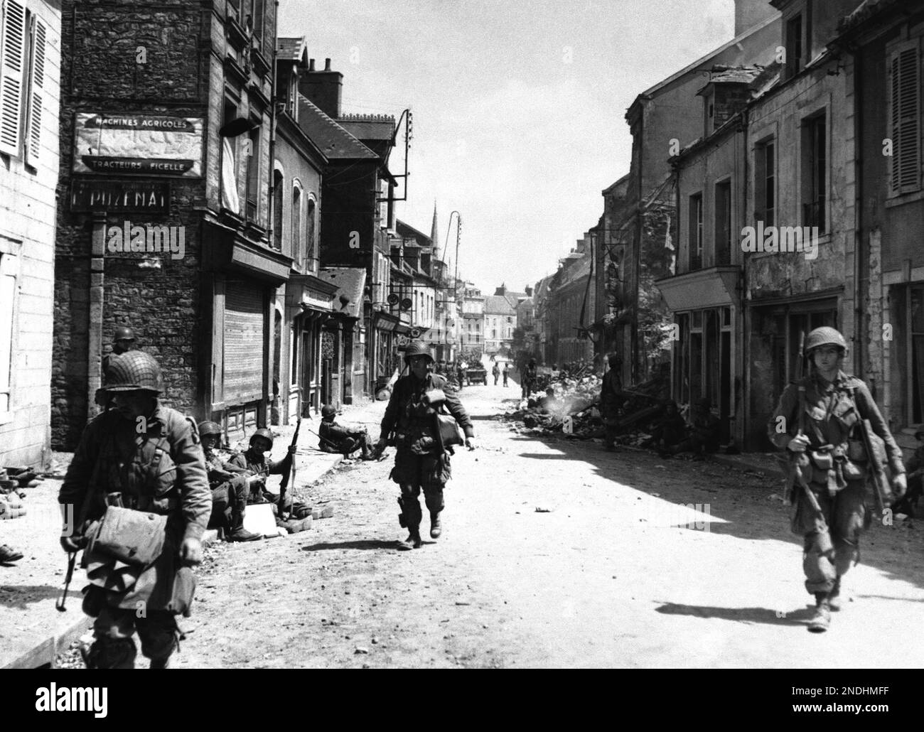 Some troops rest and others press on in one of the streets in Carentan ...