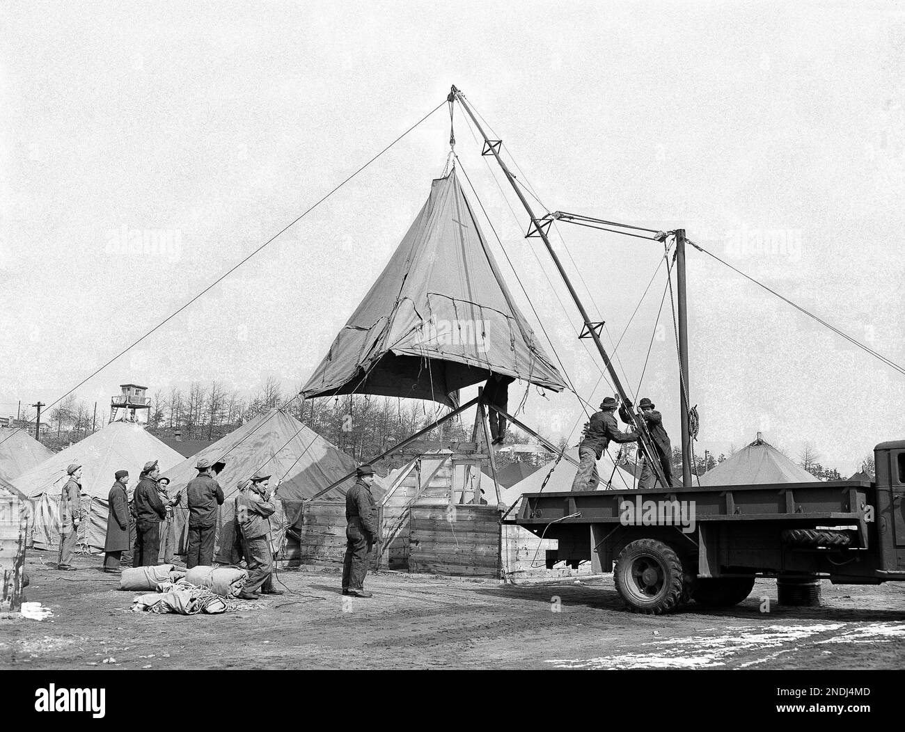 Crew of soldiers are putting the tents over wooden frames with the help ...