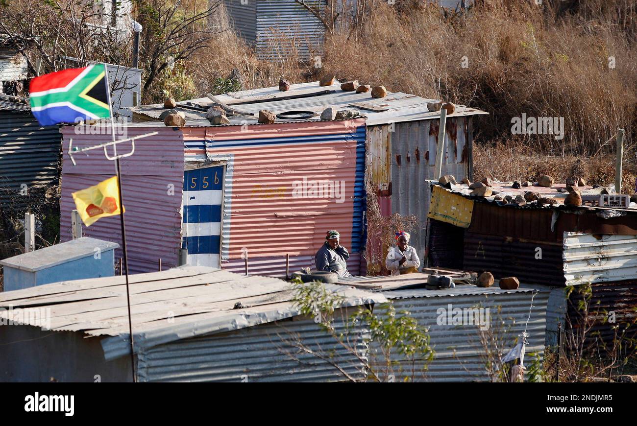 Two women sits outside their shacks at a squatter camp in Soweto ...