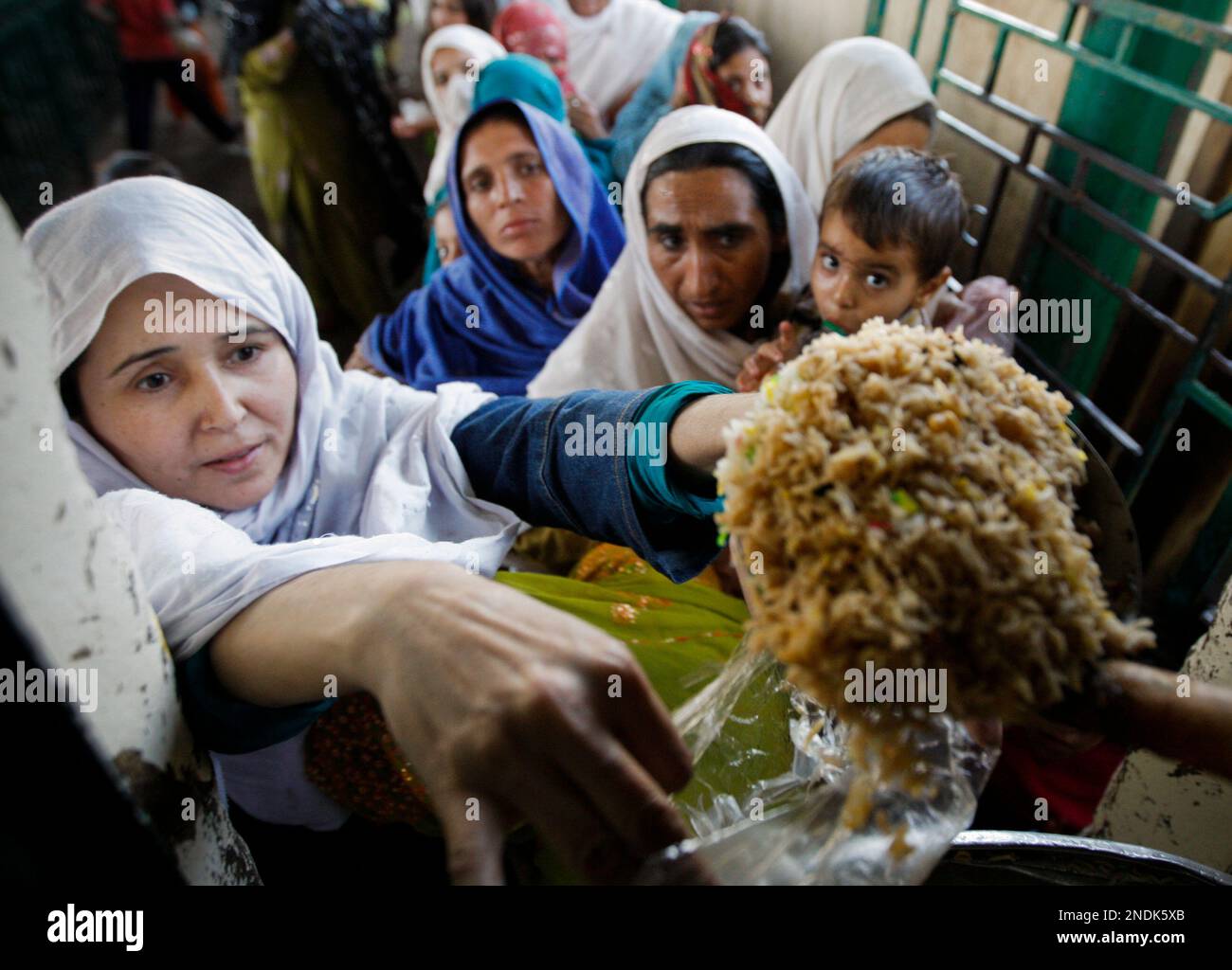 Pakistani women line up to receive a ration of donated rice at the Sufi ...