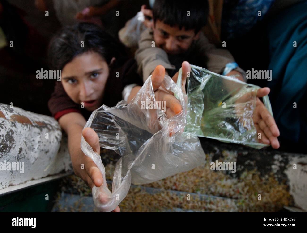 Pakistani child raise their plastic bags to receive a ration of donated ...