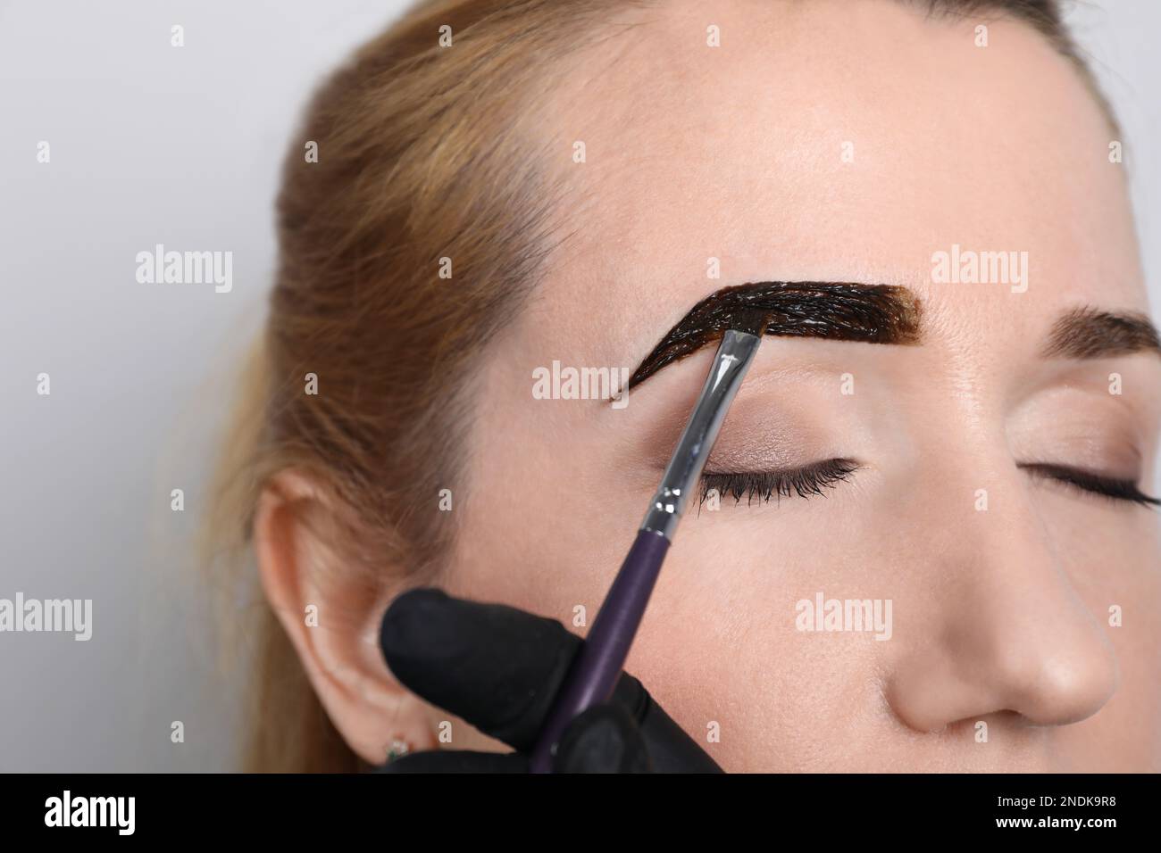 Beautician applying tint during eyebrows correction procedure on light ...