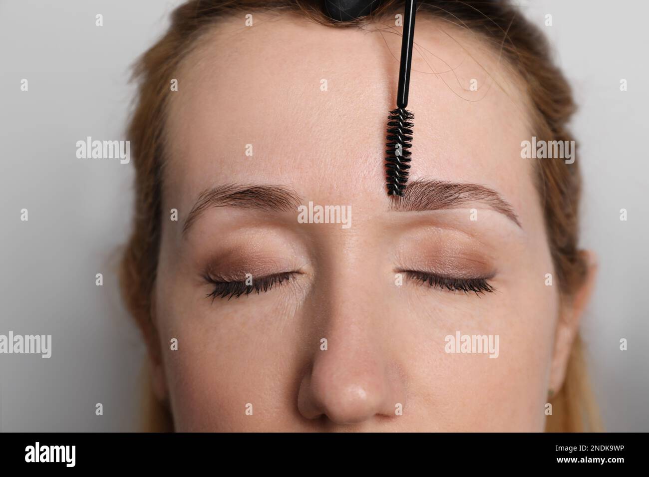 Beautician brushing woman's eyebrows before tinting on light grey ...