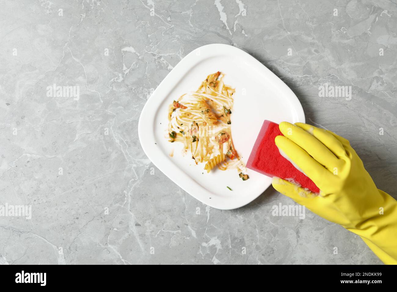 Woman washing dirty plate at grey marble table, top view. Space for ...