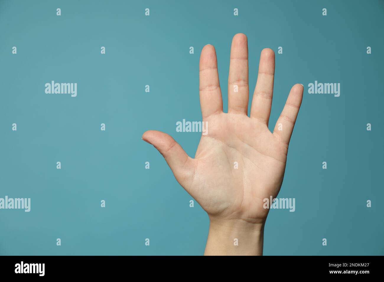 Left-handed woman holding open palm on light blue background, closeup ...