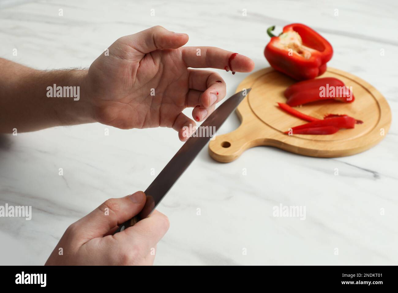 Man cut finger with knife while cooking at white marble table, closeup ...