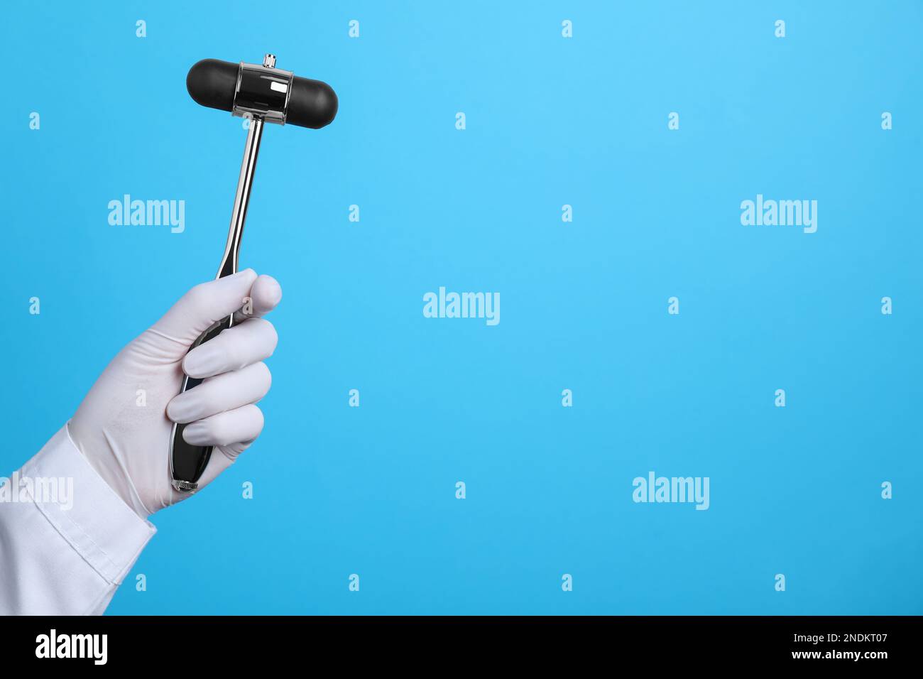 Doctor holding reflex hammer on light blue background, closeup with ...