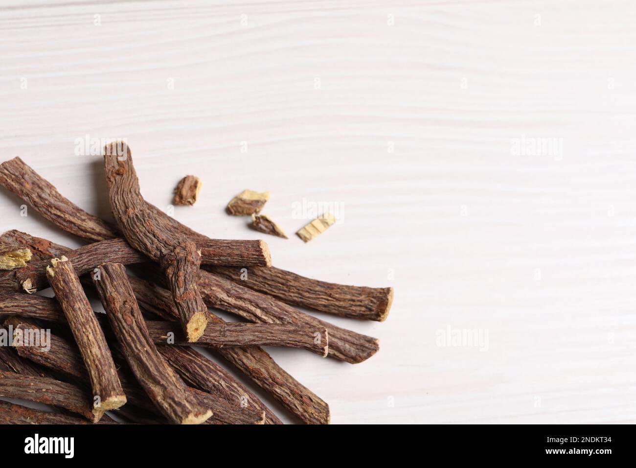 Dried sticks of liquorice root on white wooden table, space for text ...