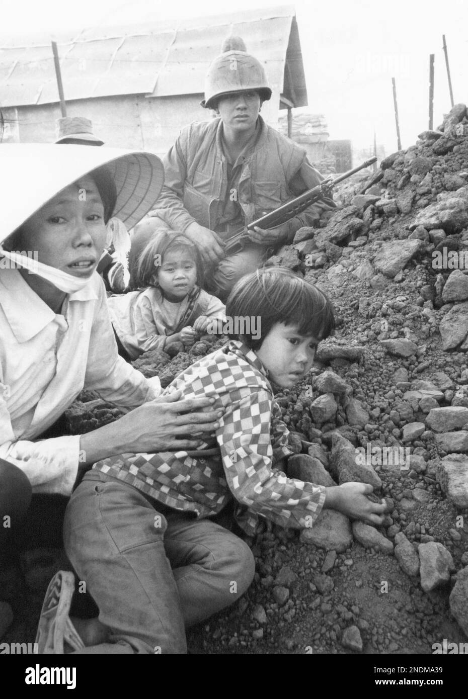 Vietnamese refugees and a U.S. marine crouch behind earth wall as North ...