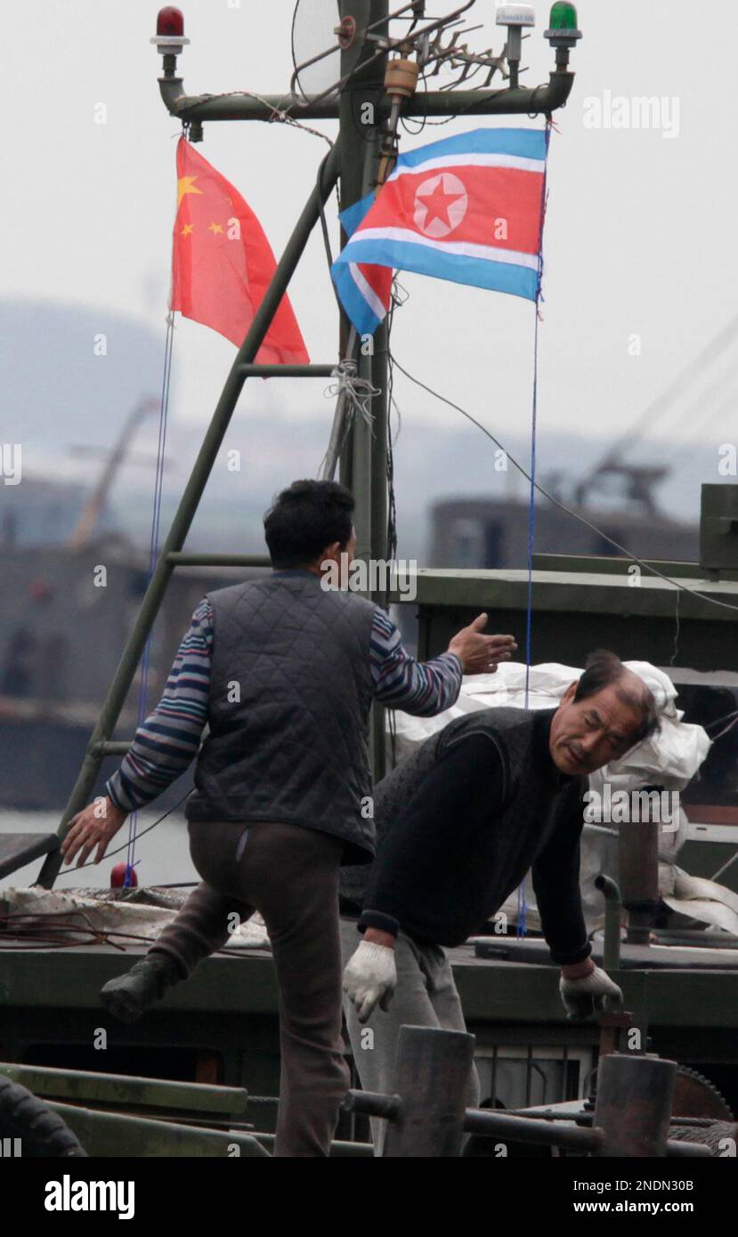A man gestures towards another onboard a boat marked with both Chinese ...