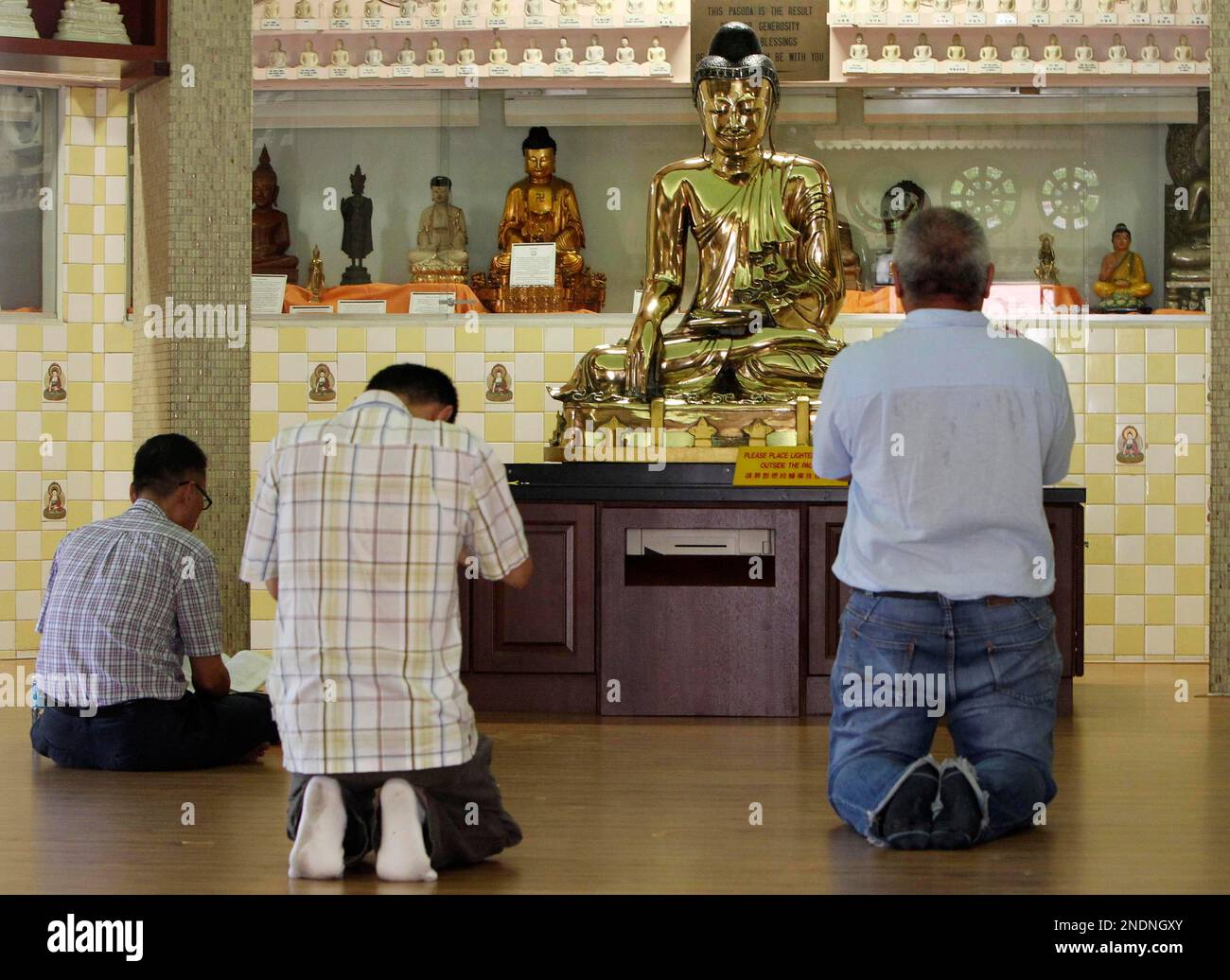 Devotees pray in front of a gold Buddha at the Buddhist Maha Vihara ...
