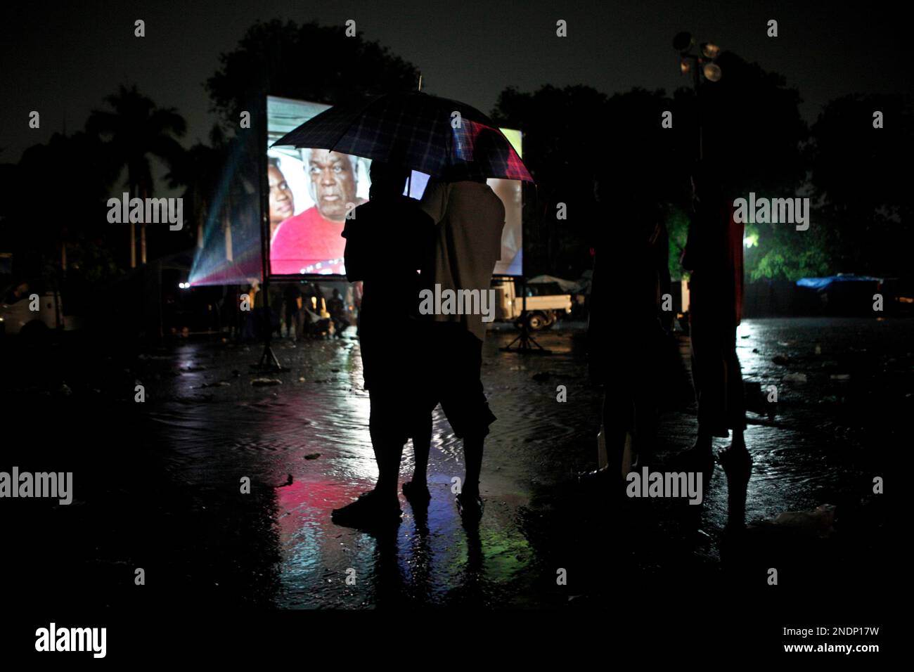 People watch a soap opera on a screen under rain at a camp for ...