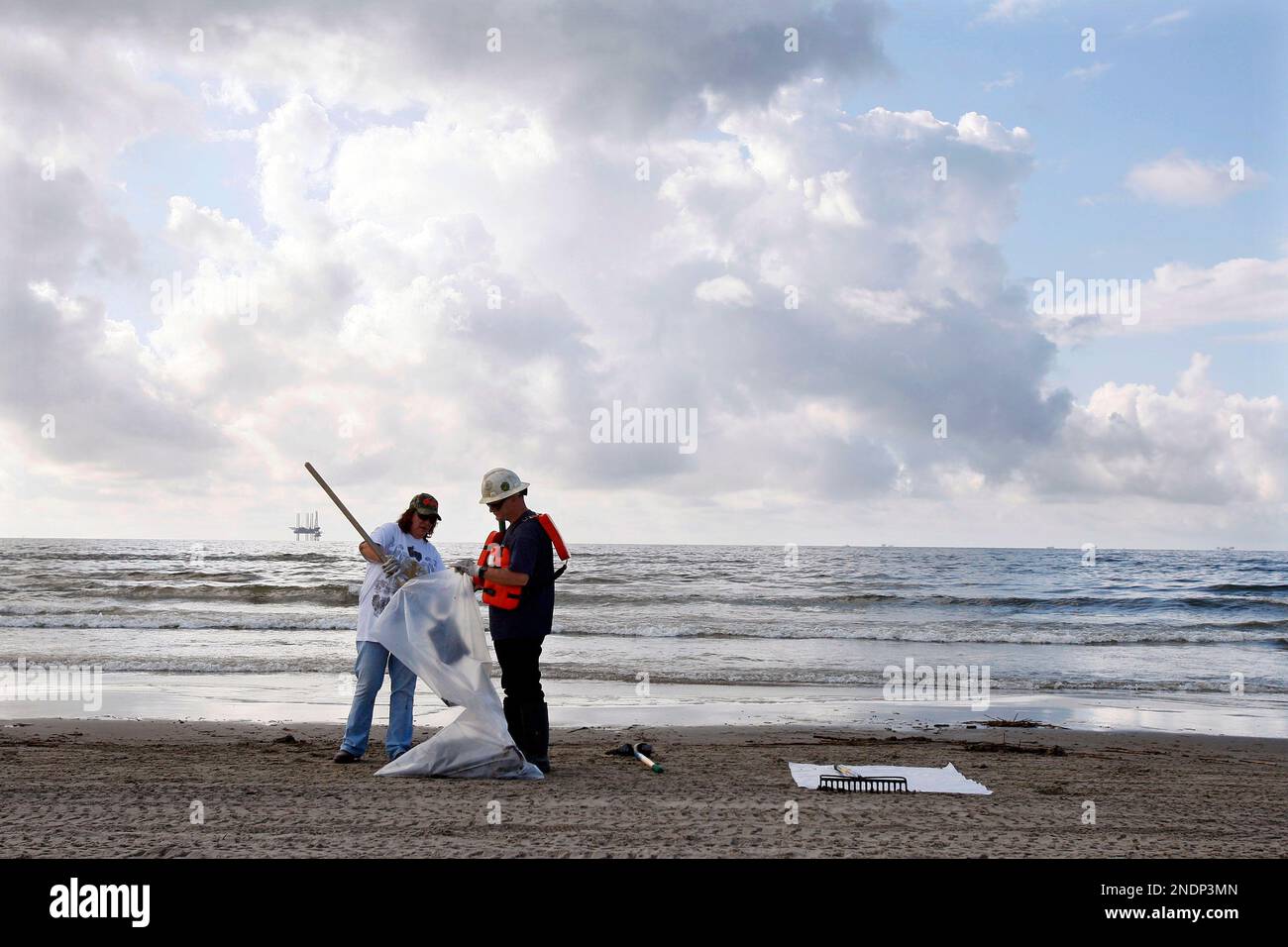 Workers collect oil and debris that washed up onto a beach in Grand ...