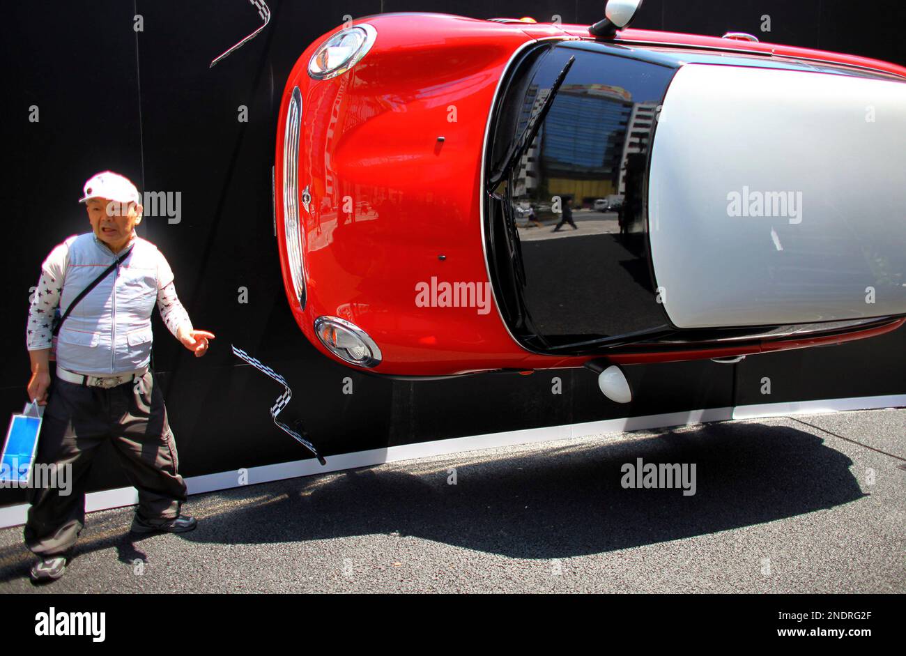 A man stands near a life size model of a MINI Cooper on display outside ...