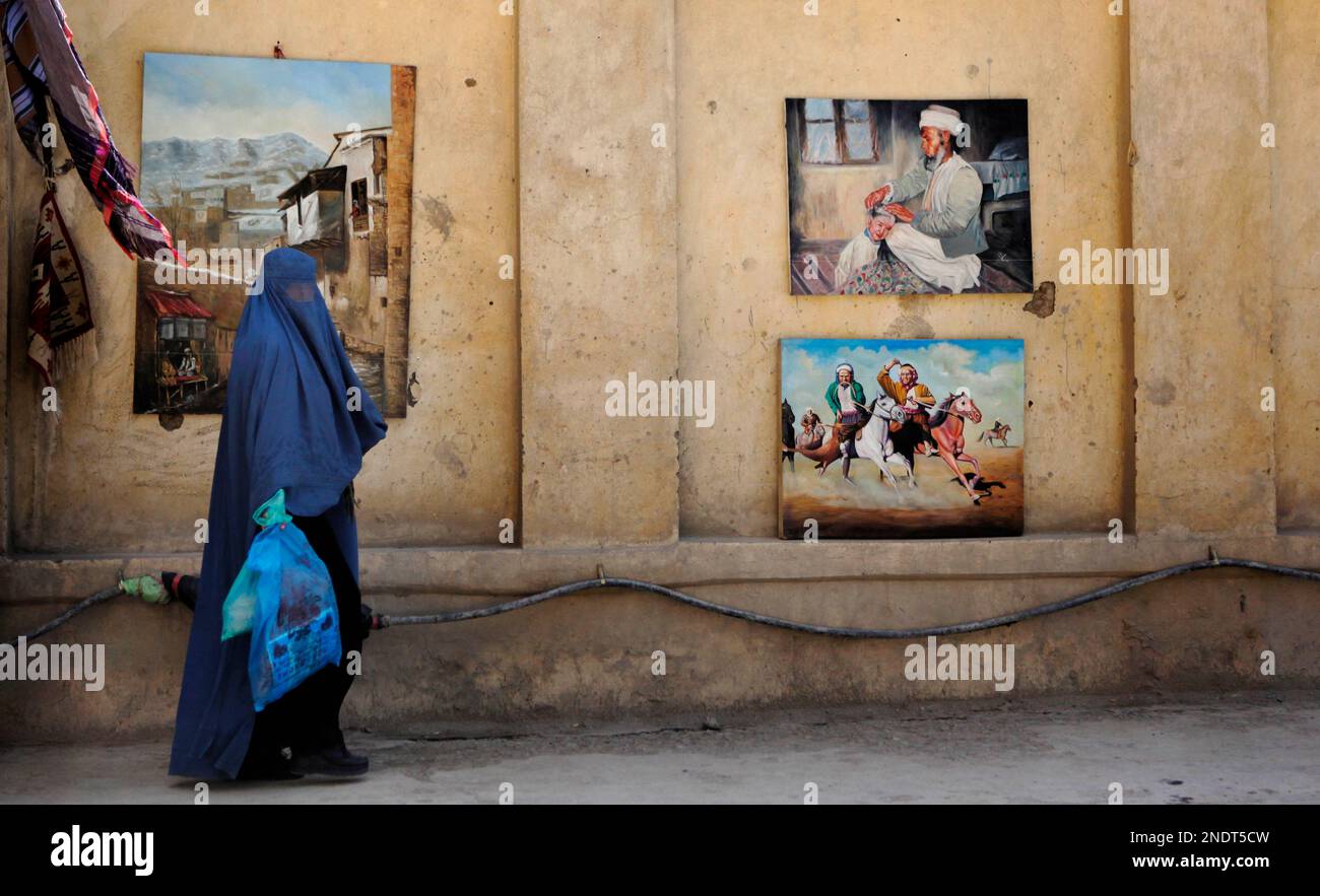 A burqa-clad Afghan woman walks past paintings hanging on a wall for ...