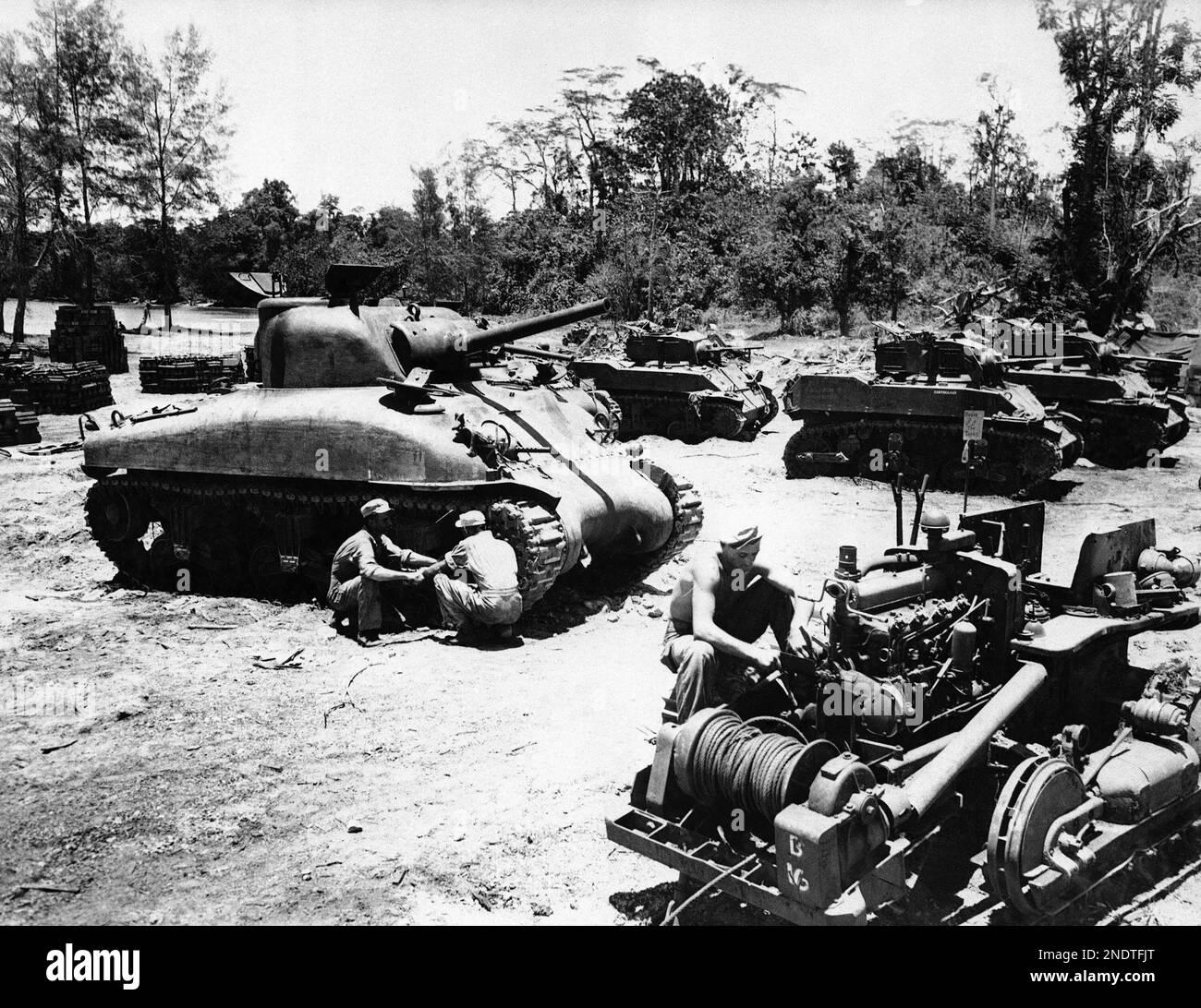 Army ordnance men work on a medium tank and a tractor put out of action ...