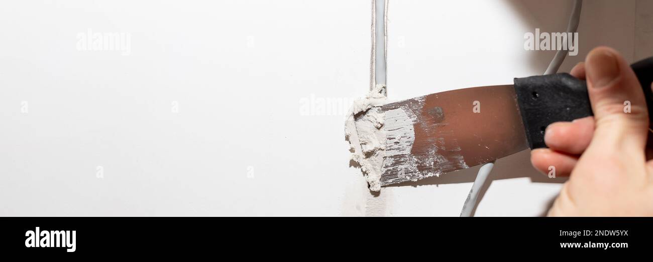 Worker fixing cracks on ceiling, spreading plaster using trowel ...