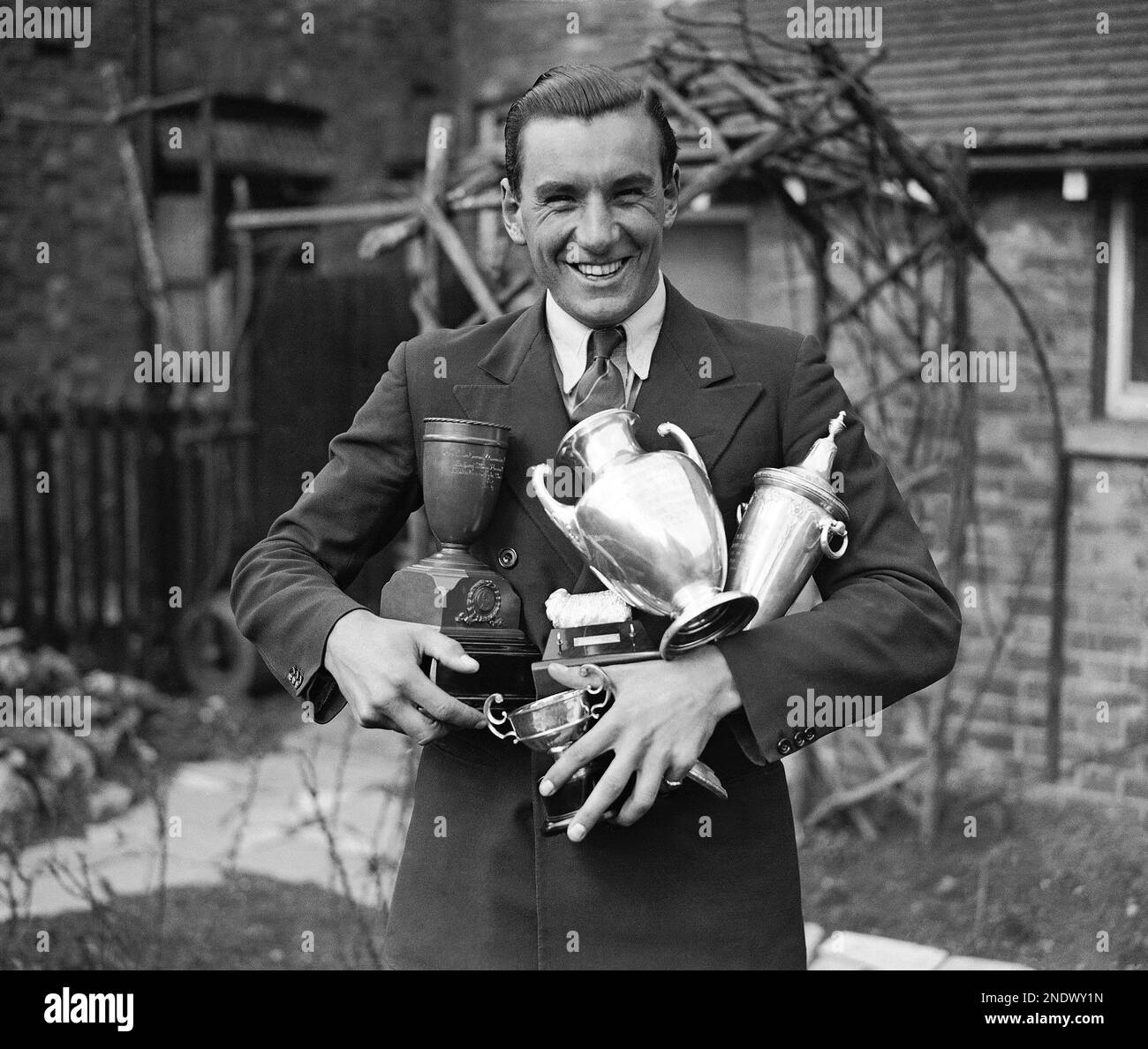 British tennis player Fred Perry with an armful of his trophies won ...