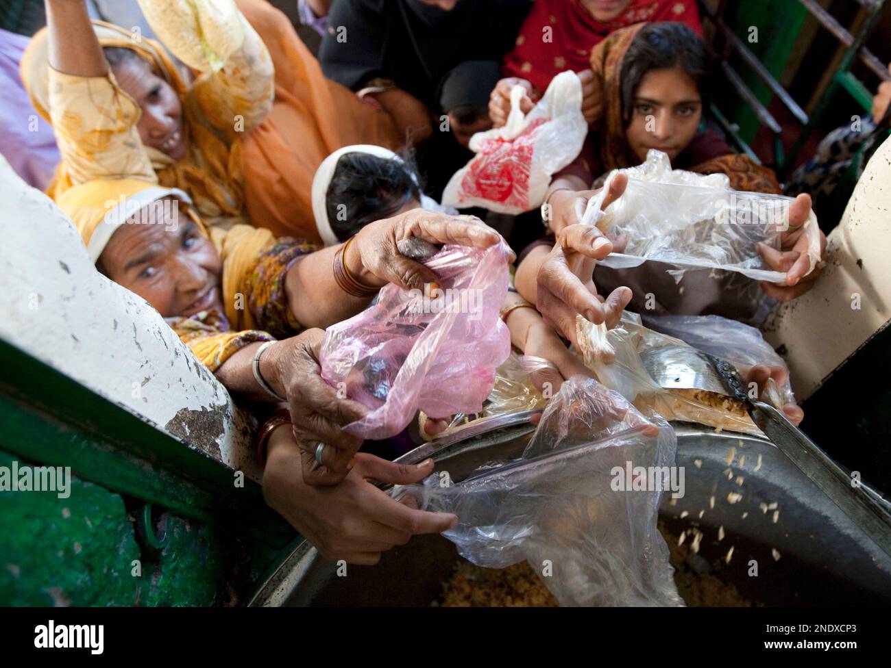 Pakistani women raise their plastic bags to receive a ration of donated ...