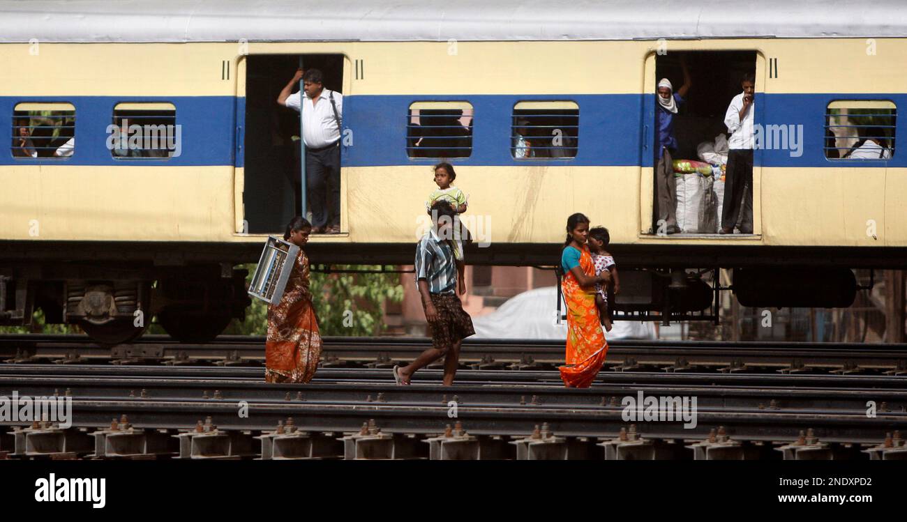 A family walks on railway tracks, as a local train passes by in New ...