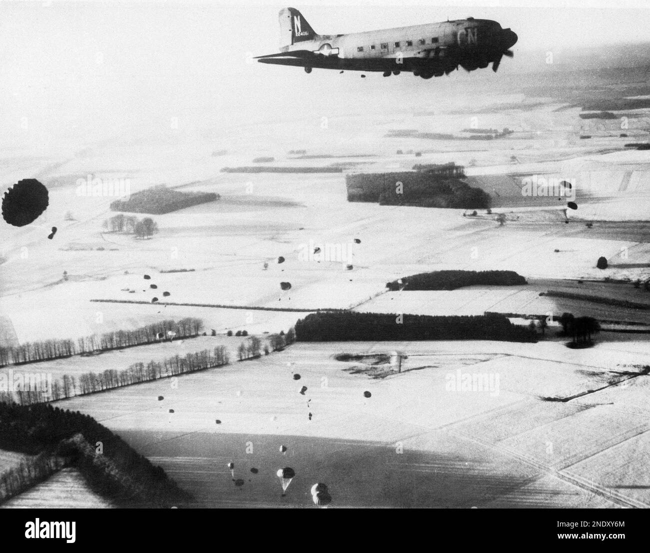 A U.S. troop carrier plane drops a parapack which drifts down to the ...