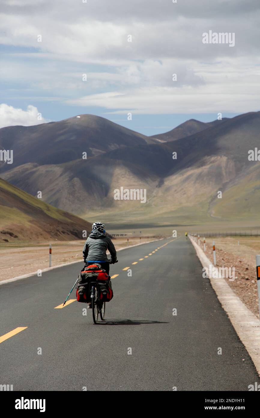 A human riding bicycle on road through desert surrounded by hills Stock ...