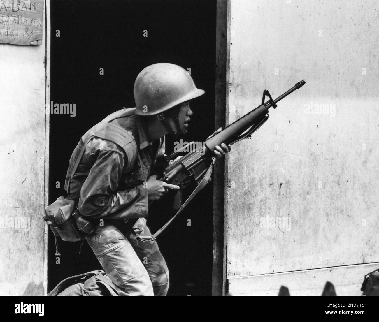 A South Vietnamese soldier, his weapon at the ready, looks out of a ...